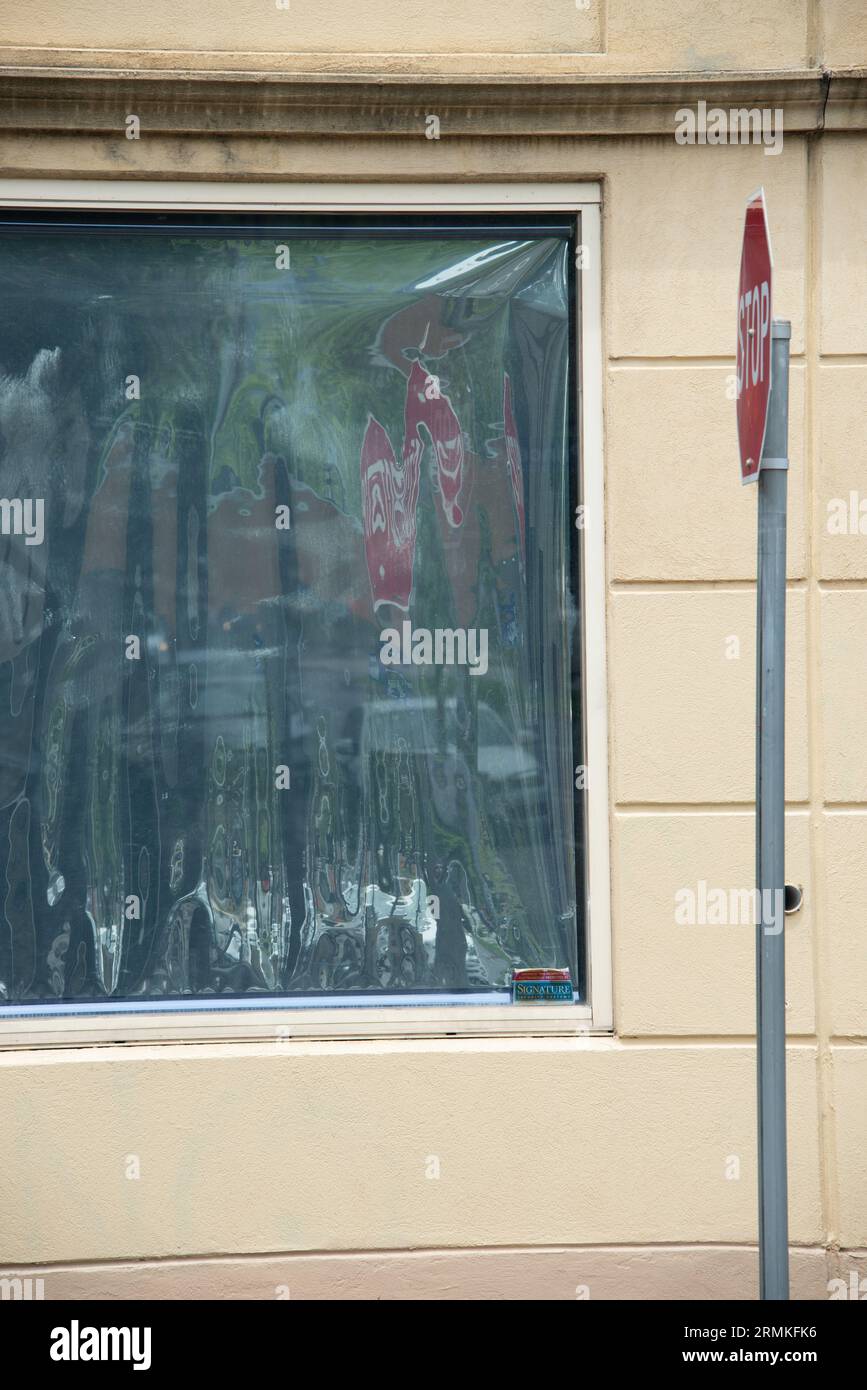 A stop sign reflected in a window and also visible in the foreground ...