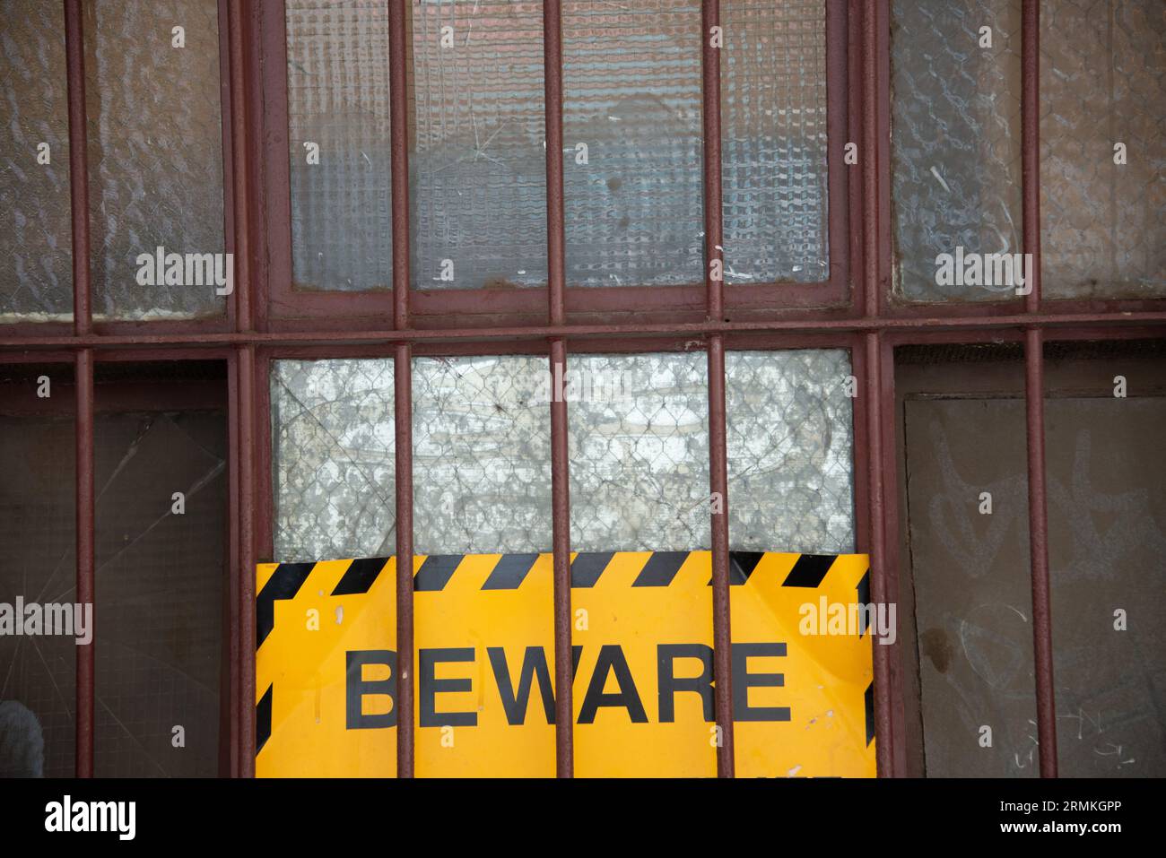 A yellow and black Beware sign on the barred window of an old factory ...