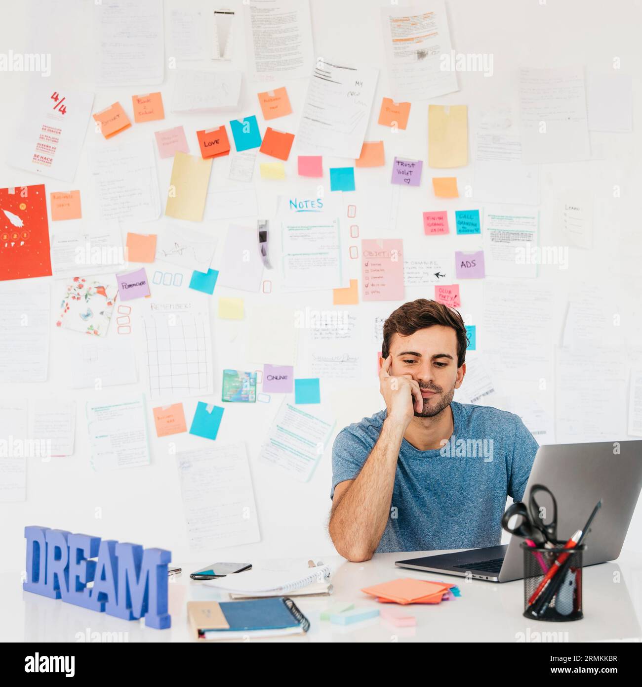 Tired young man sitting near laptop against wall with notes Stock Photo ...