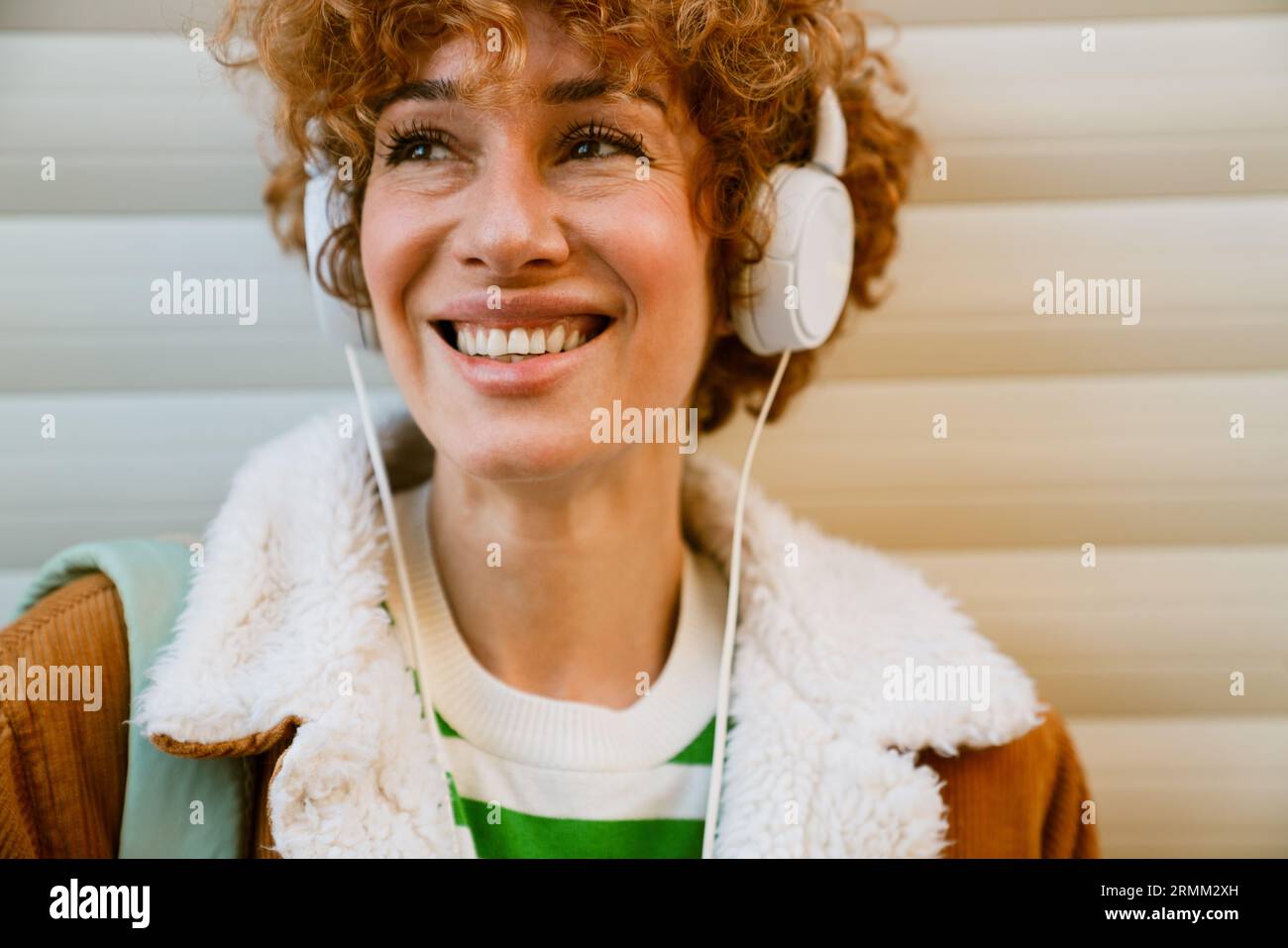 Mid white woman with curly hair using headphones while standing over ...