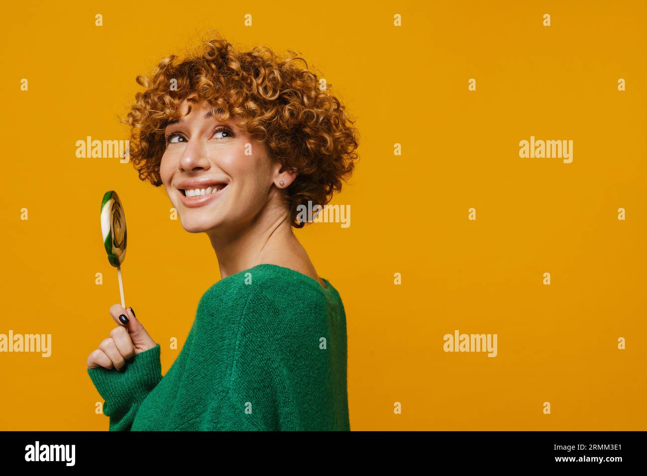 Cheerful middle-aged ginger woman posing with lollipop isolated over ...