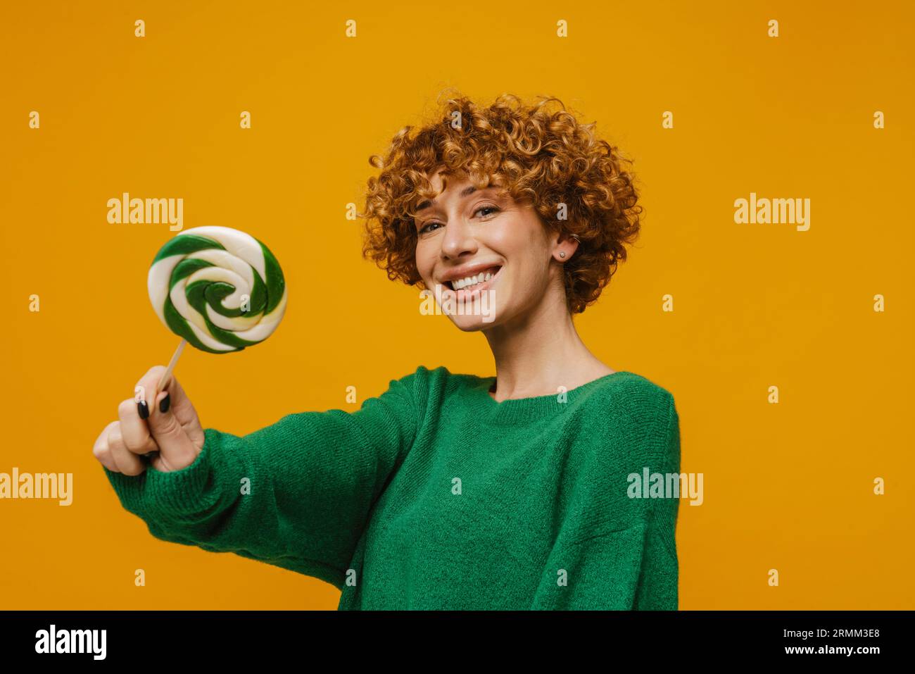 Middle-aged ginger woman posing with lollipop isolated over yellow ...
