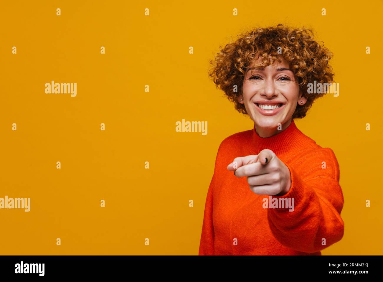 Cheerful curly middle-aged woman pointing finger at you isolated over ...