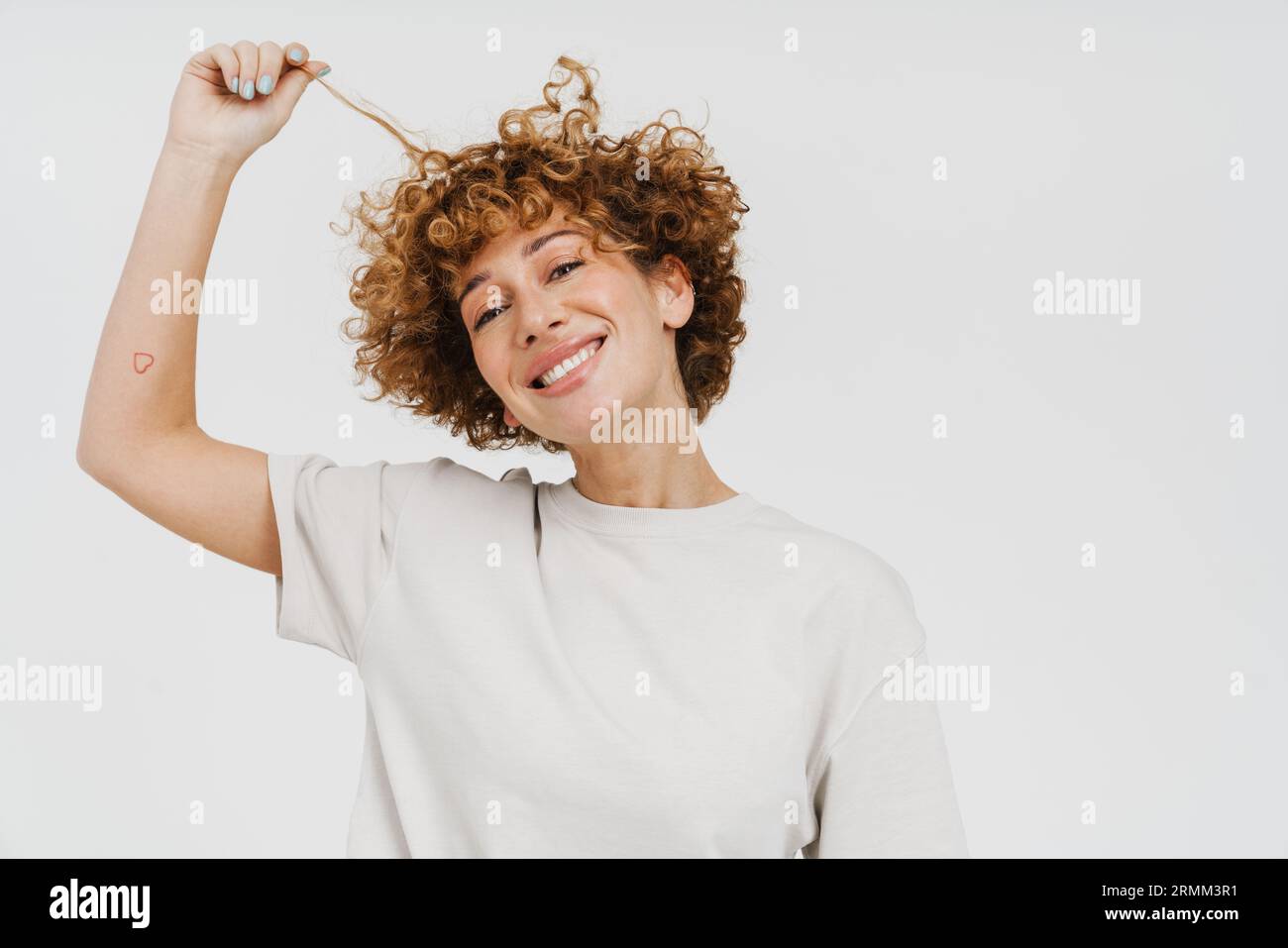 Middle-aged ginger woman smiling and touching hair isolated over white ...
