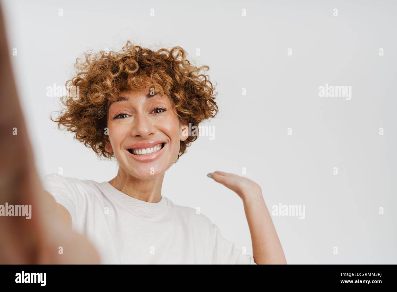 Middle-aged ginger woman waving while taking selfie isolated over white ...