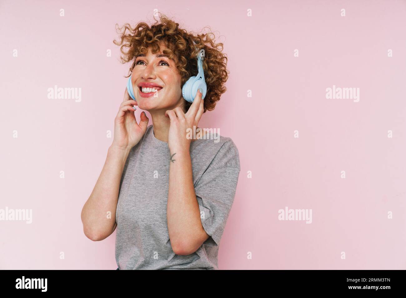 Cheerful middle-aged ginger woman listening music with headphones ...