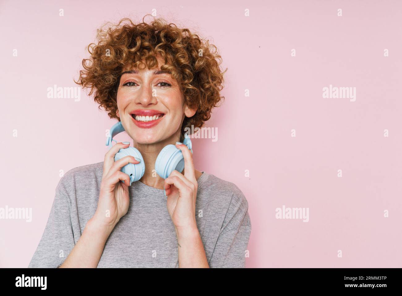Cheerful middle-aged ginger woman listening music with headphones ...