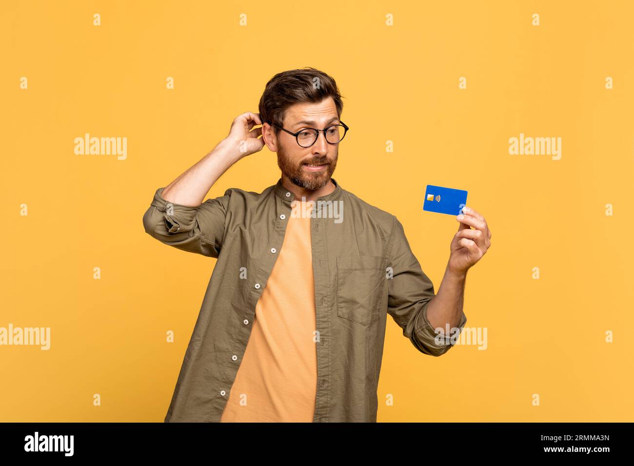 Pensive middle aged man scratching head, look at credit card and think ...