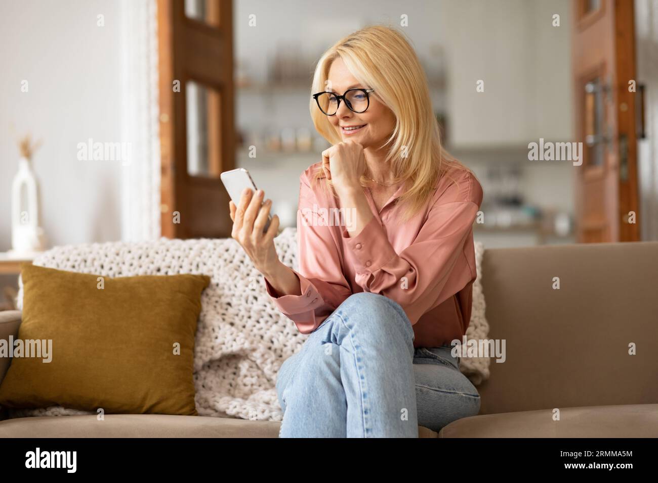 Mature lady using cellphone, wearing glasses and having chat indoors ...