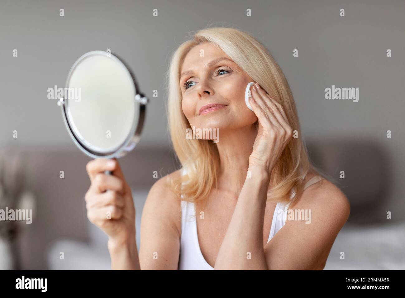 Beautiful middle aged lady looking in mirror, erasing make up from her ...