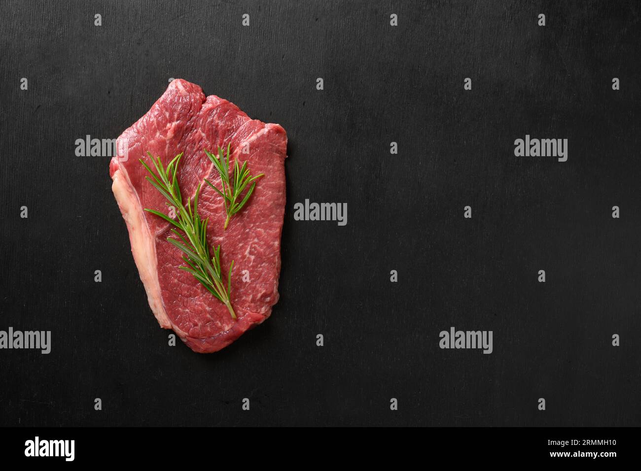 Raw marbled ribeye steak with rosemary sprig on black background. Top ...