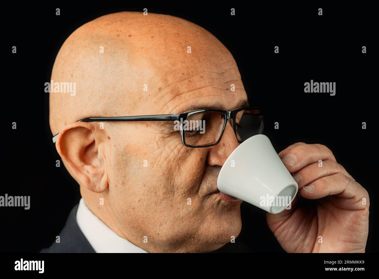 In a close-up portrait, a bald elderly gentleman fervently sips ...