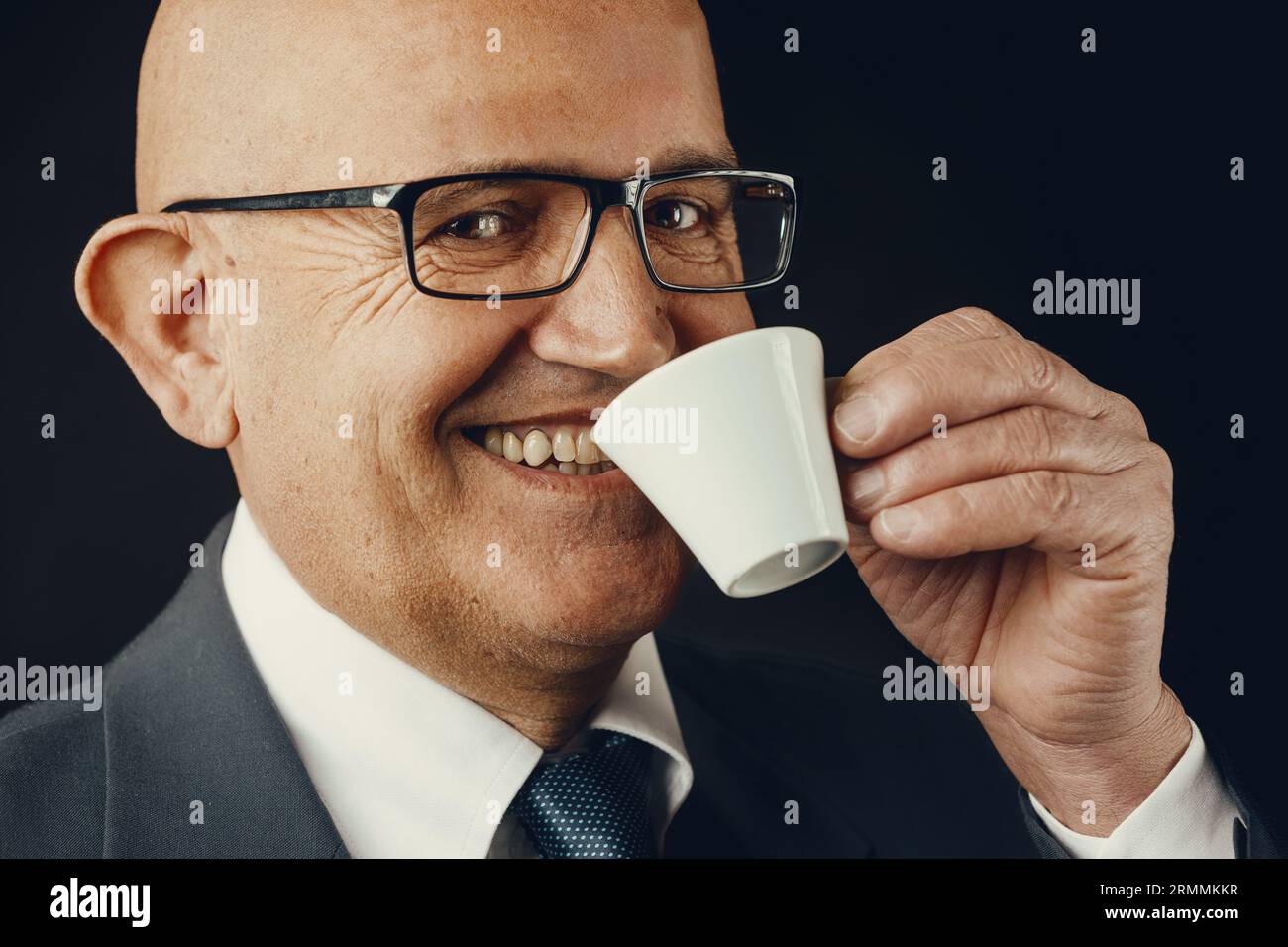 elder bald man, in a dark jacket and white shirt, sips true Italian ...