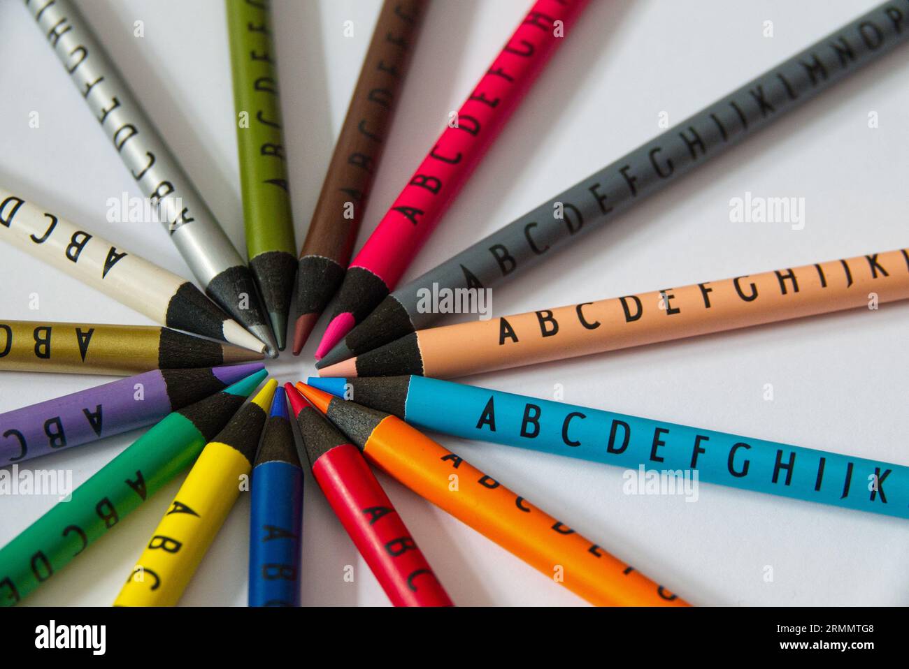 Different colored crayons with letters arranged in a circle on white ...