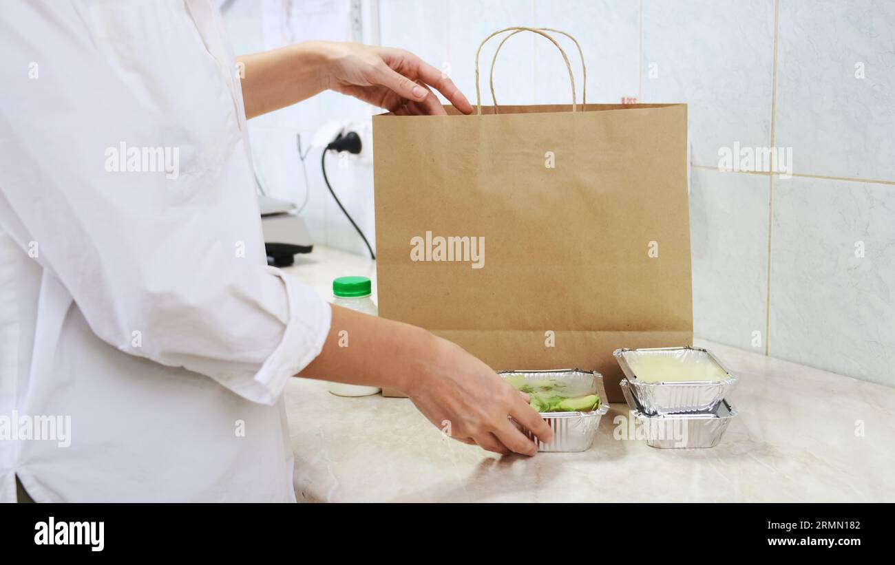 Food delivery service in restaurant. Chef packs lunch boxes to paper ...