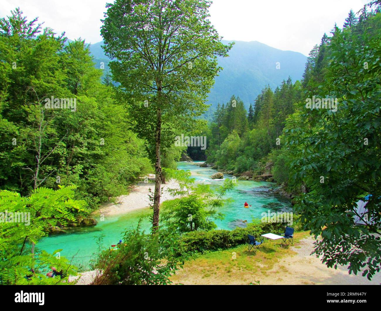 View of Soca river surrounded by woods and table with chairs in front ...