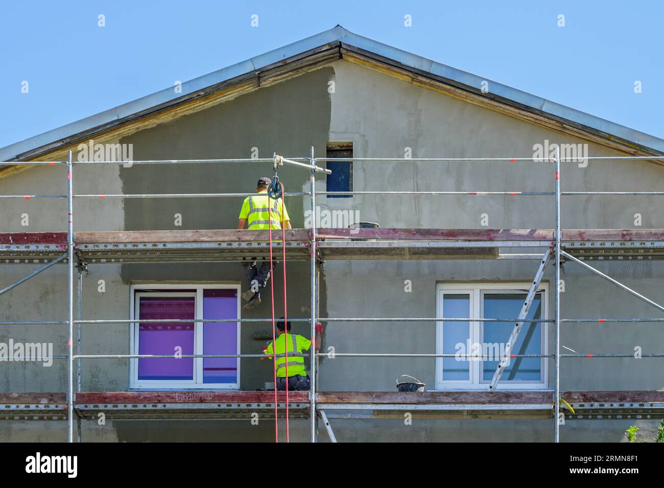 Two painters in green safety vests paint the facade of a residential ...