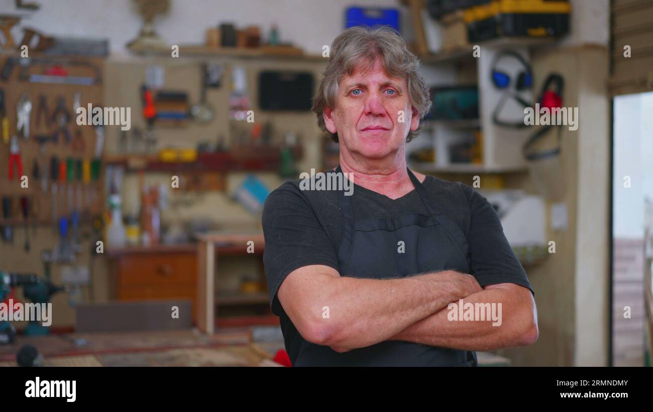 Portrait of a master carpenter standing inside workshop with arms ...