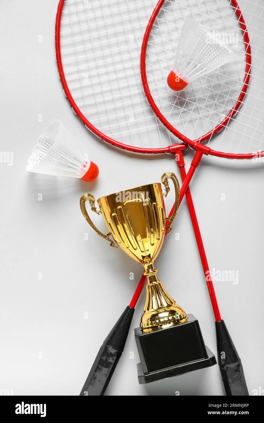Gold cup with badminton rackets and shuttlecocks on light background ...