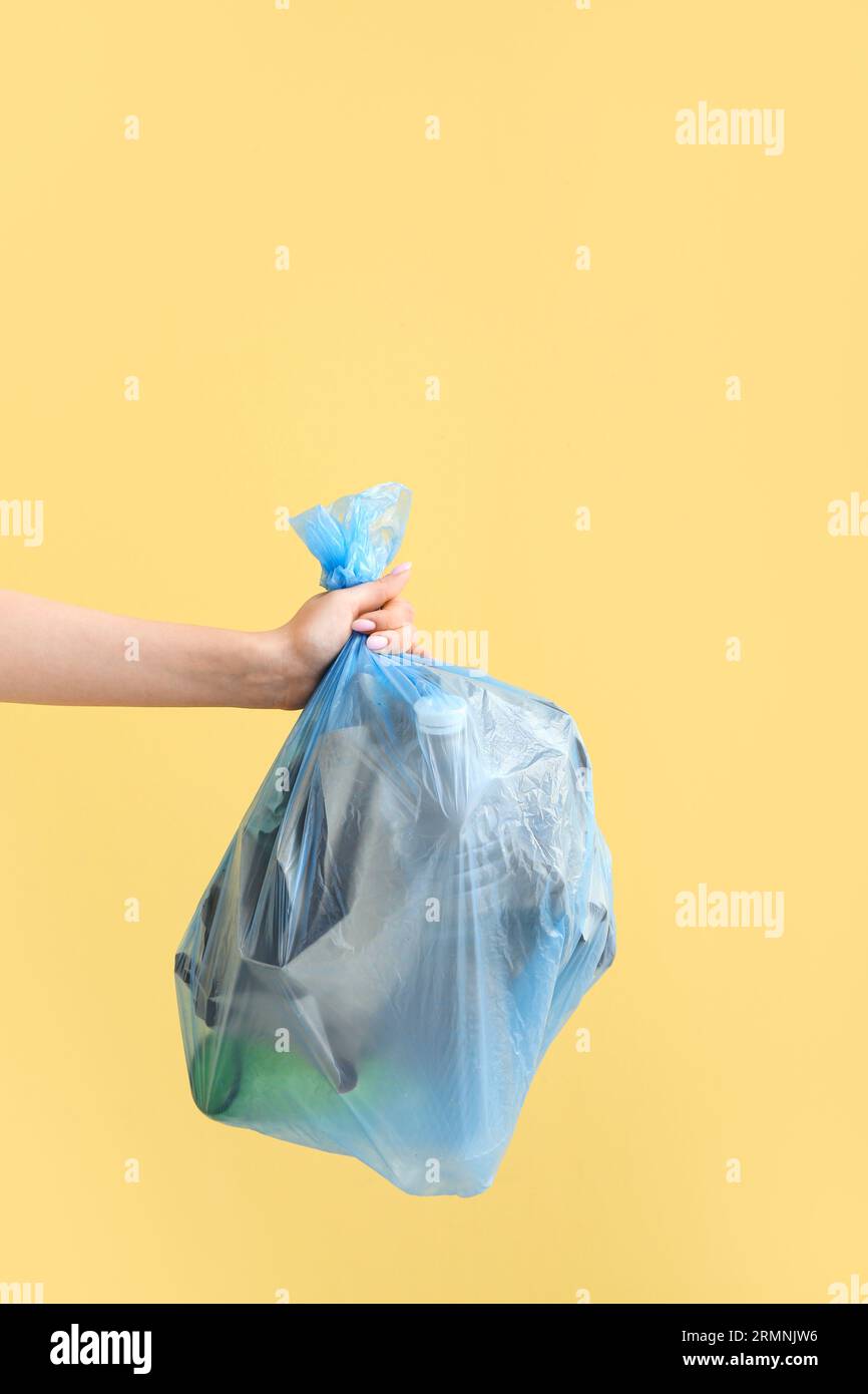 Female hand holding full garbage bag on yellow background Stock Photo ...