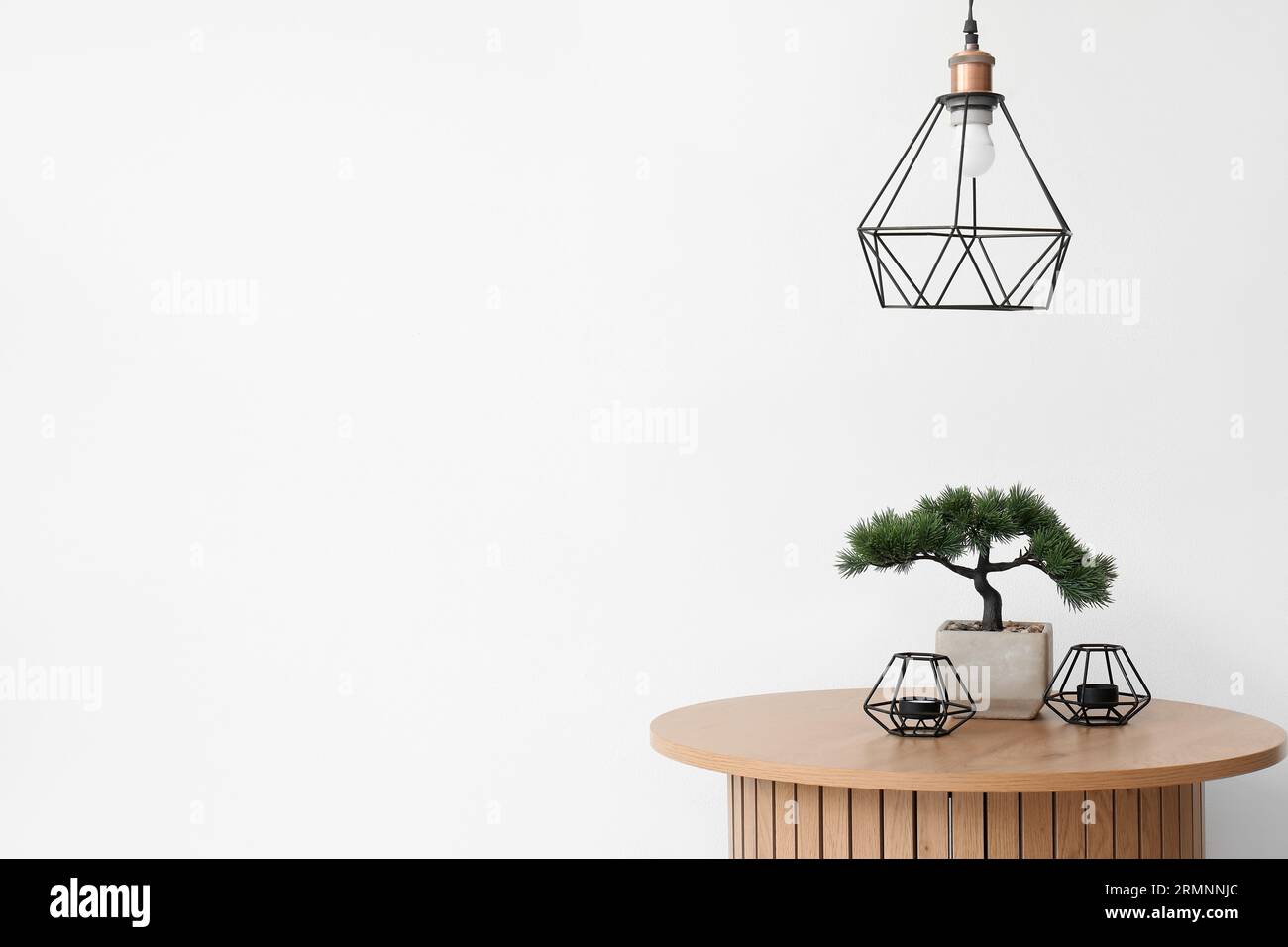 Wooden coffee table with bonsai tree and candle holders near white wall ...