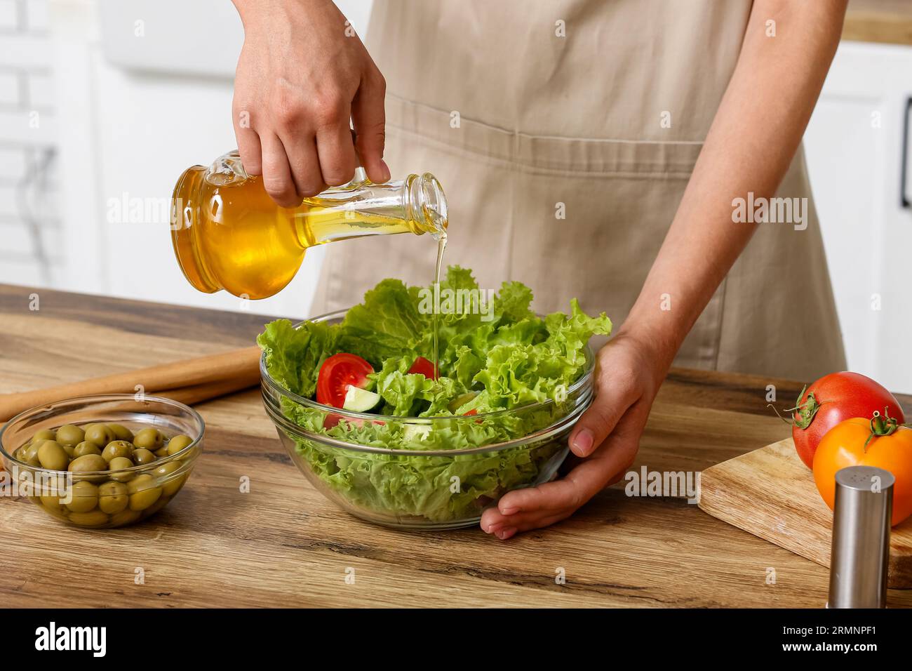 Woman adding olive oil into bowl with tasty salad at table in kitchen ...