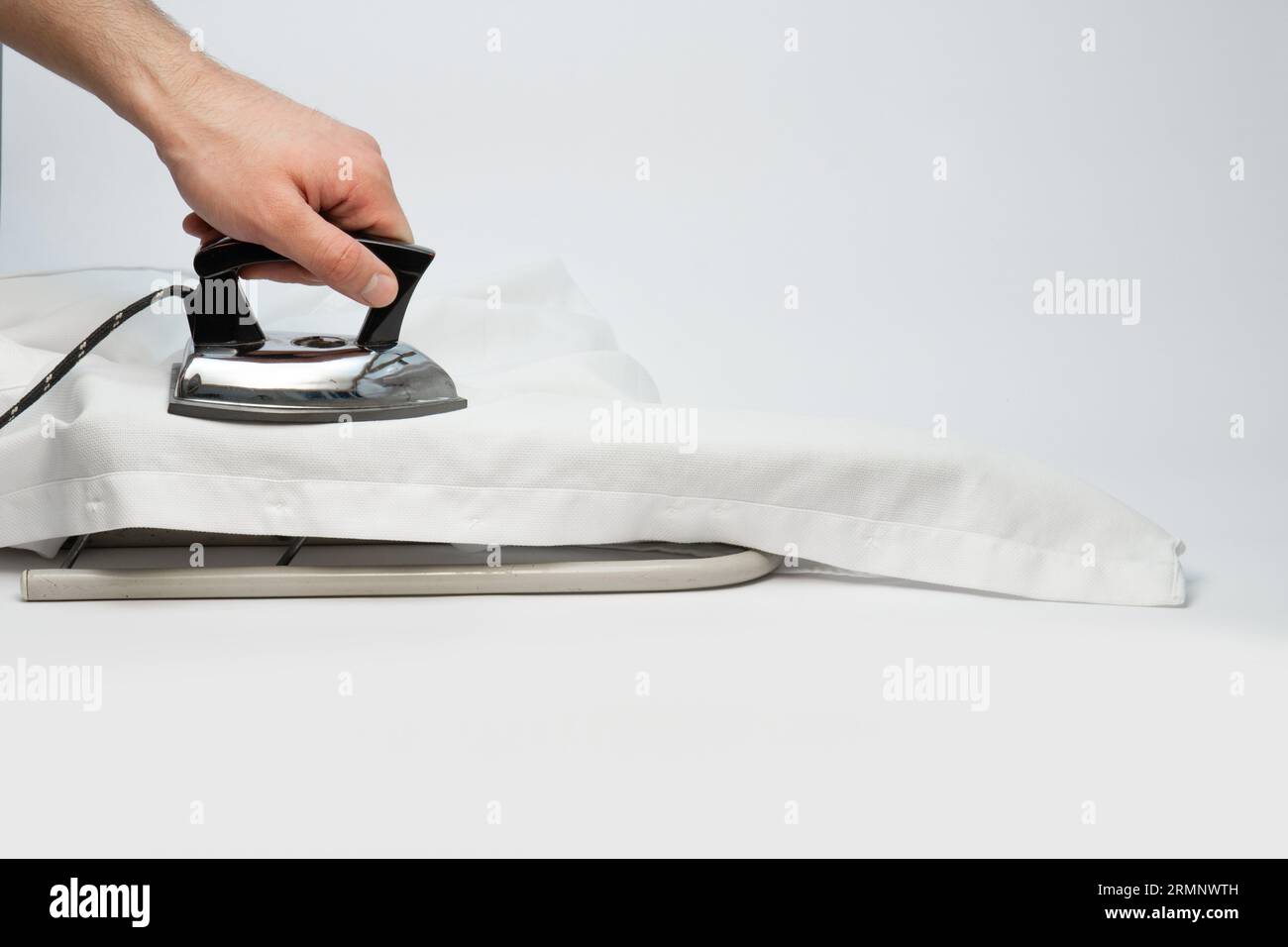 Male hand ironing white shirt with small old electric iron on small ...