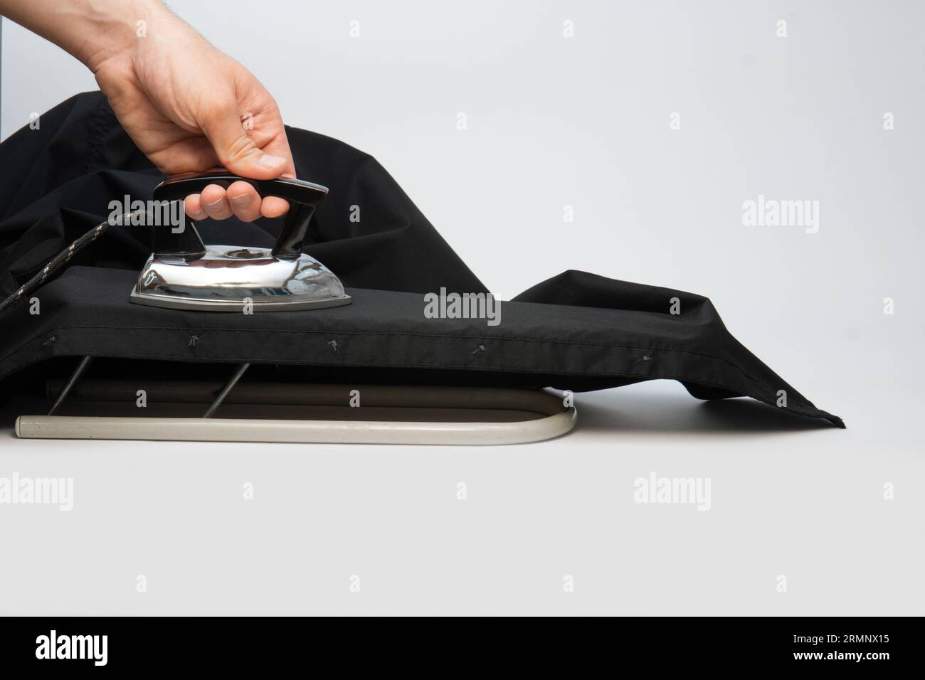 Male hand ironing black shirt with small old electric iron on small ...