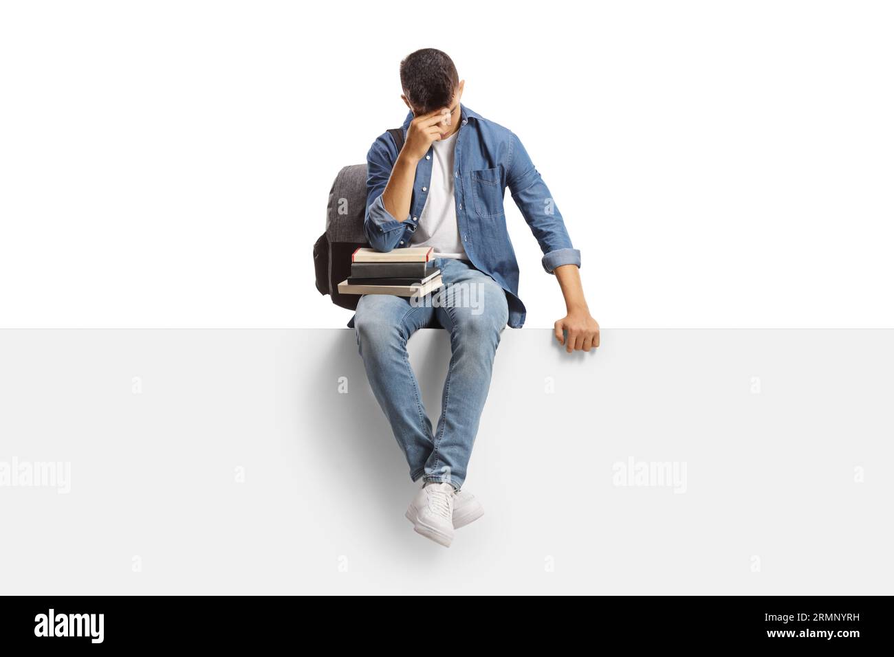 Disappointed male student sitting on a blank panel isolated on white ...