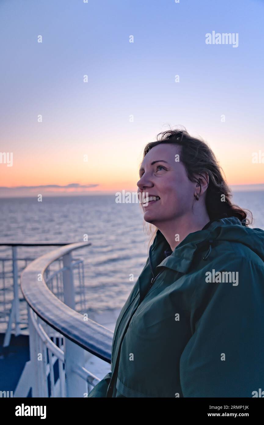 Beautiful woman leaning against boat railing looking at the glowing ...