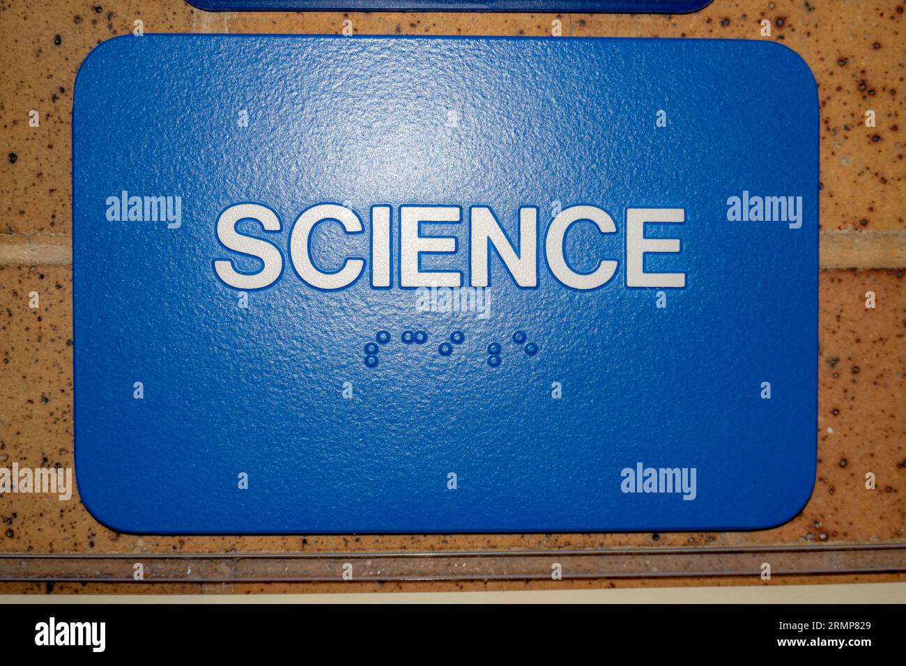 Blue science sign with braille, on brick wall at door to school office ...