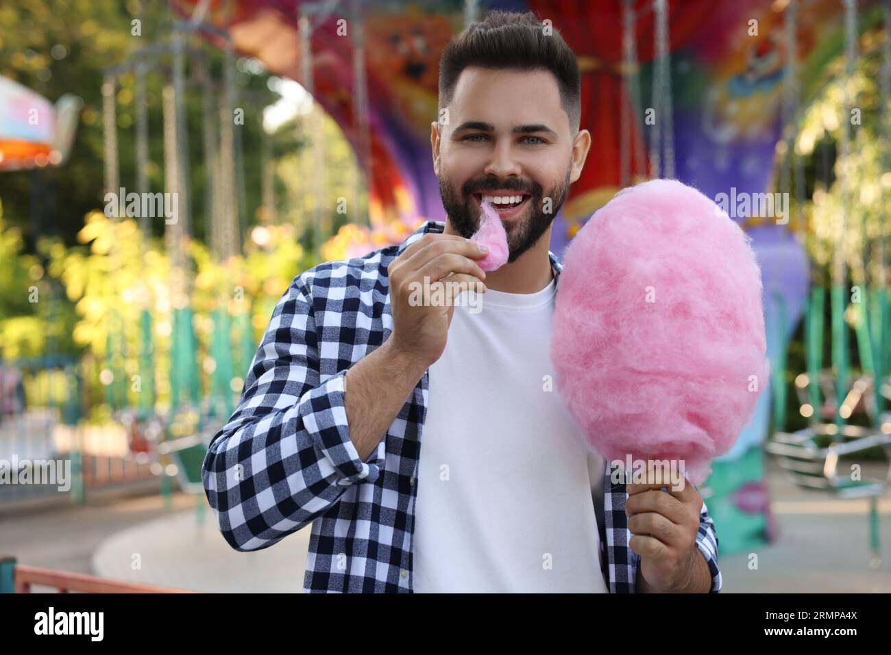 Happy young man eating cotton candy at funfair Stock Photo - Alamy