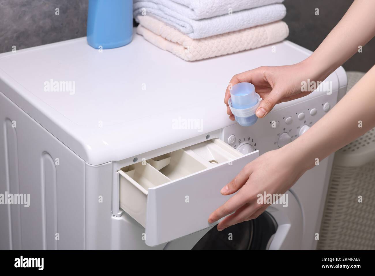 Woman pouring fabric softener from cap into washing machine, closeup ...