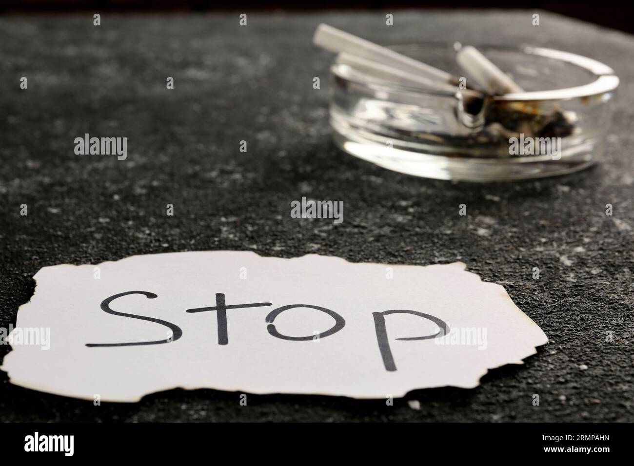 Ashtray with burnt cigarettes and word Stop written on paper on black ...