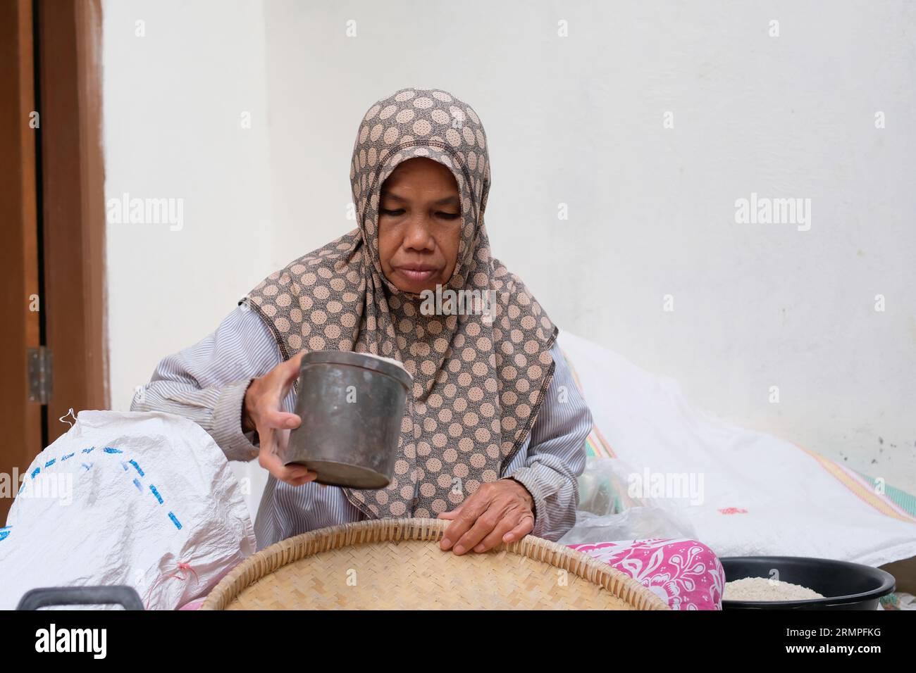 Asian old woman winnowing rice using a traditional basket to clean the ...