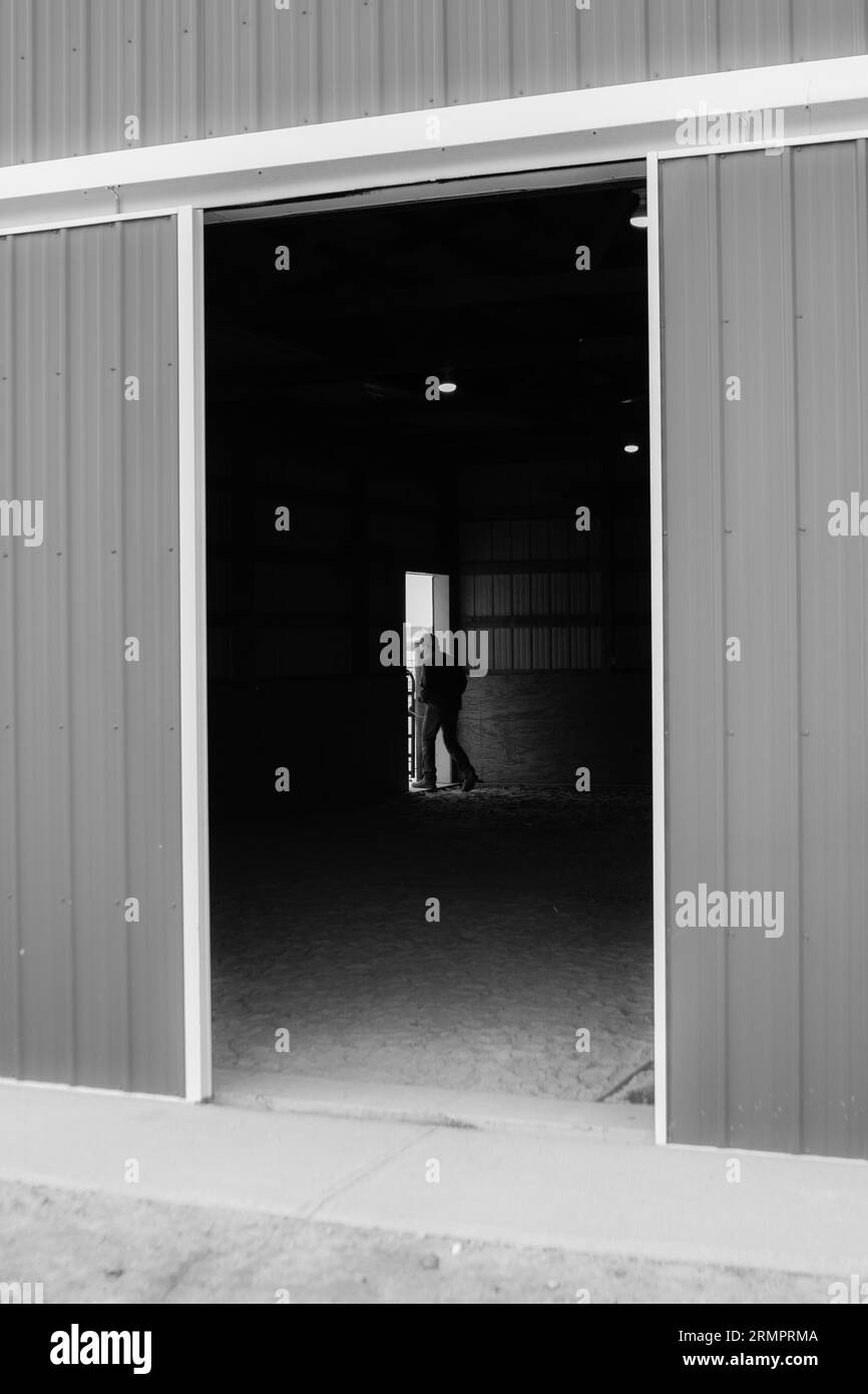 A man walking through an open door of a rural barn in grayscale Stock ...