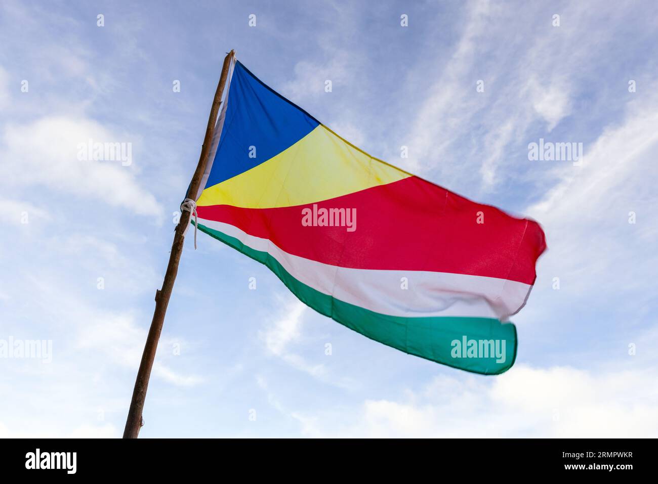 The flag of Seychelles waving in wind under cloudy blue sky on a sunny ...
