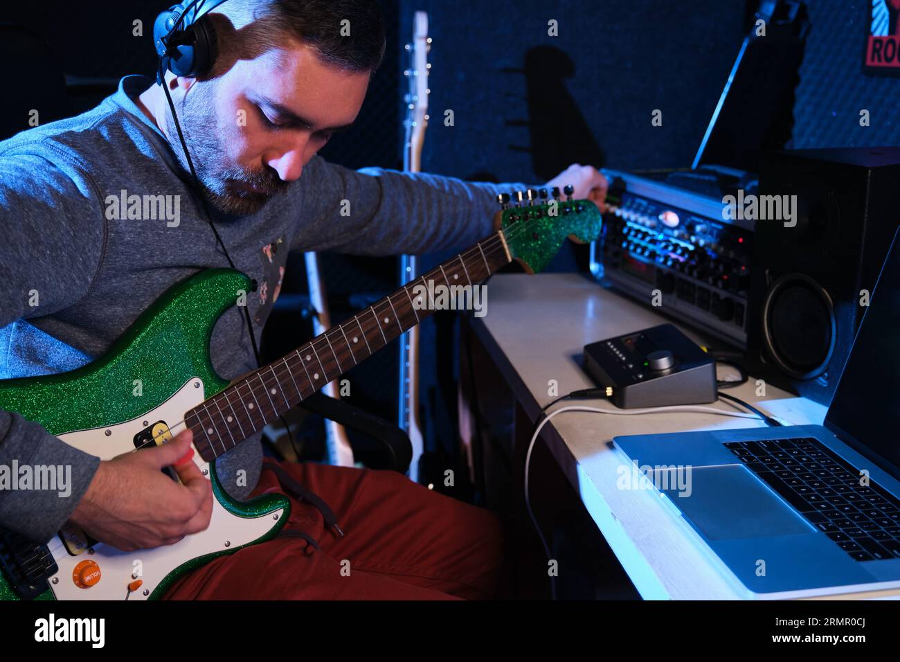 Musician man tuning his electric guitar with mixing console at home ...