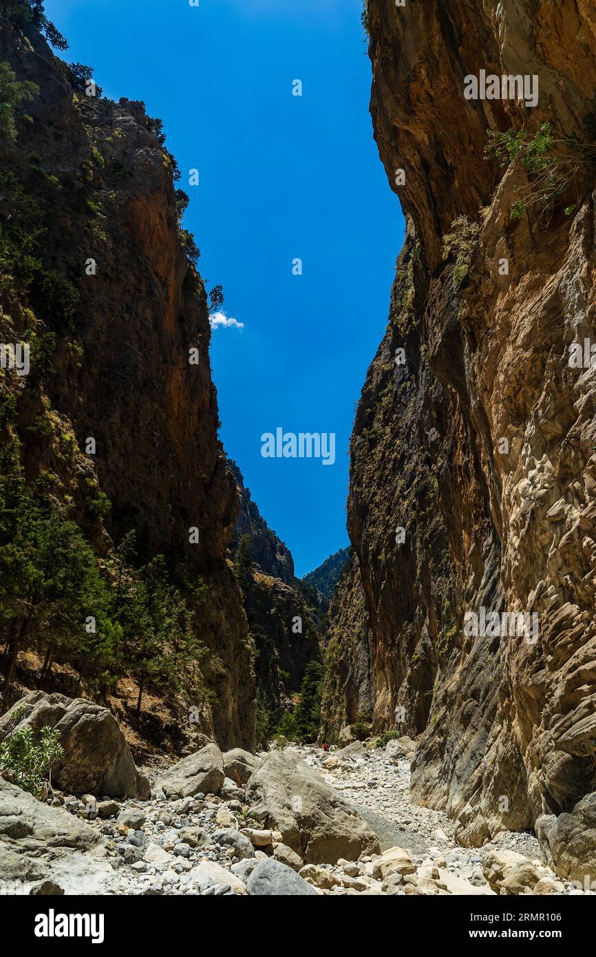 Towering vertical cliffs and a rocky, dry riverbed in the Samaria Gorge ...