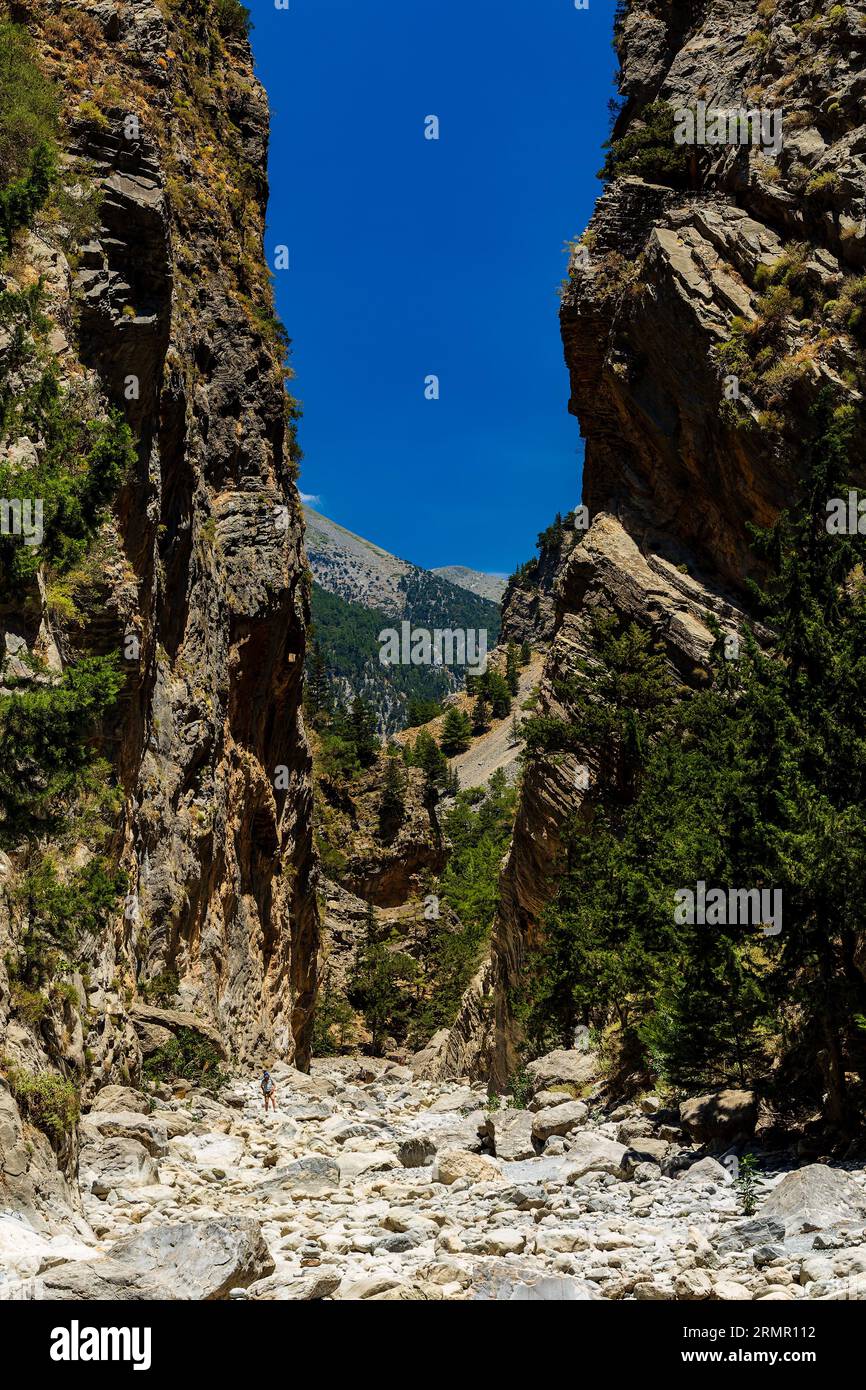 Towering vertical cliffs and a rocky, dry riverbed in the Samaria Gorge ...