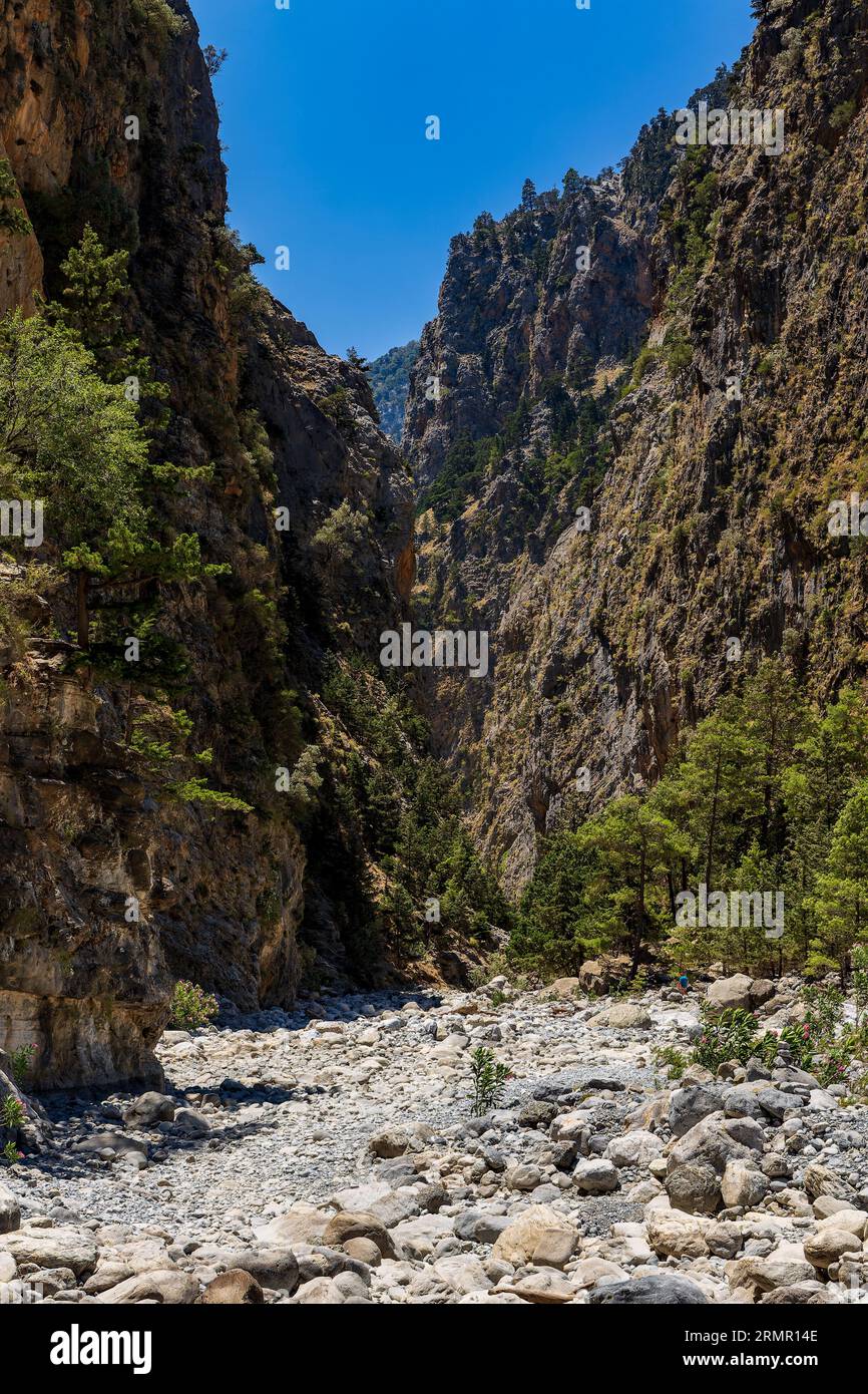 Towering vertical cliffs and a rocky, dry riverbed in the Samaria Gorge ...