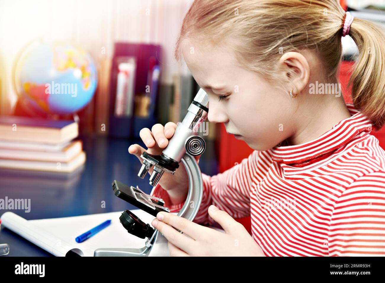 Girl looking through microscope at home learning table Stock Photo - Alamy