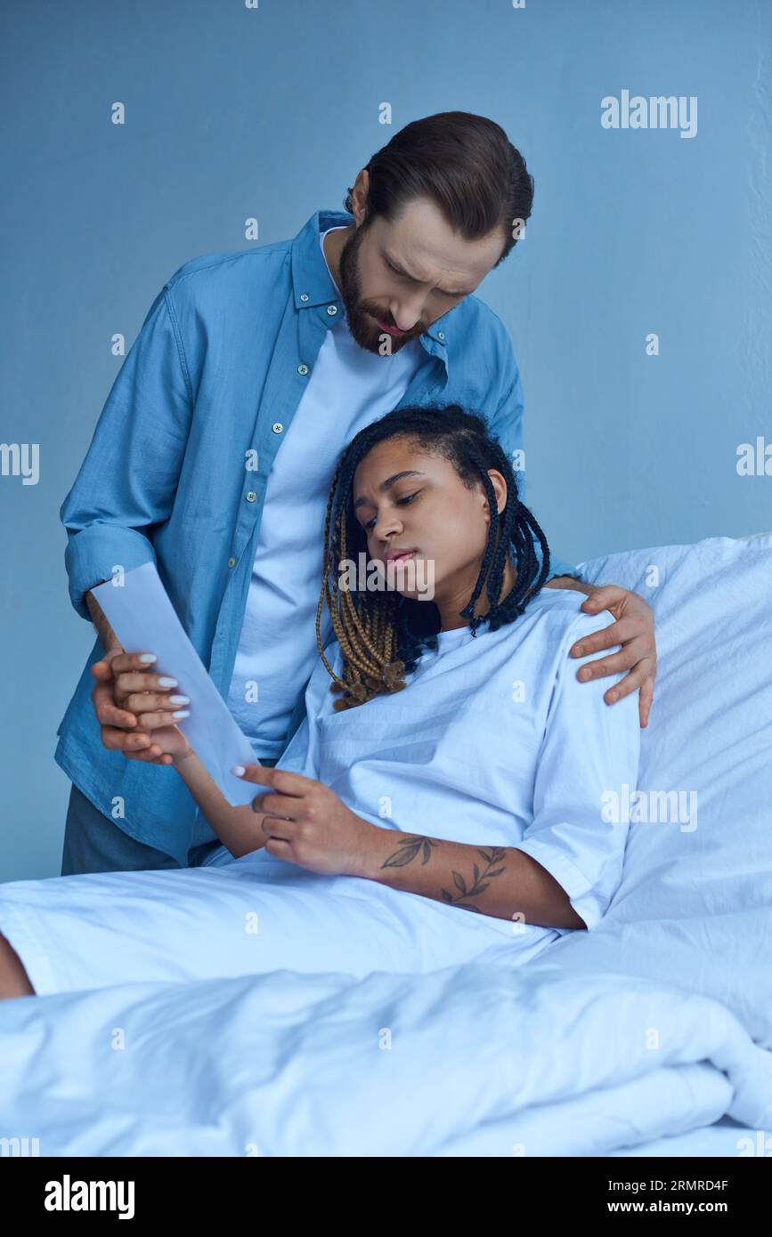 Sad Man Standing Near African American Wife Looking At Ultrasound