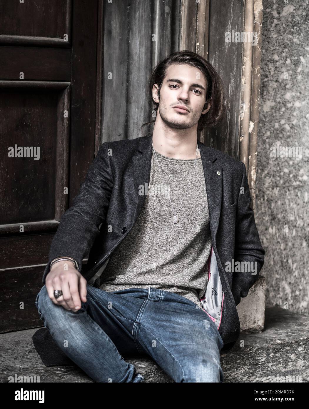 A man sitting on the ground in front of a door. Photo of a man sitting ...