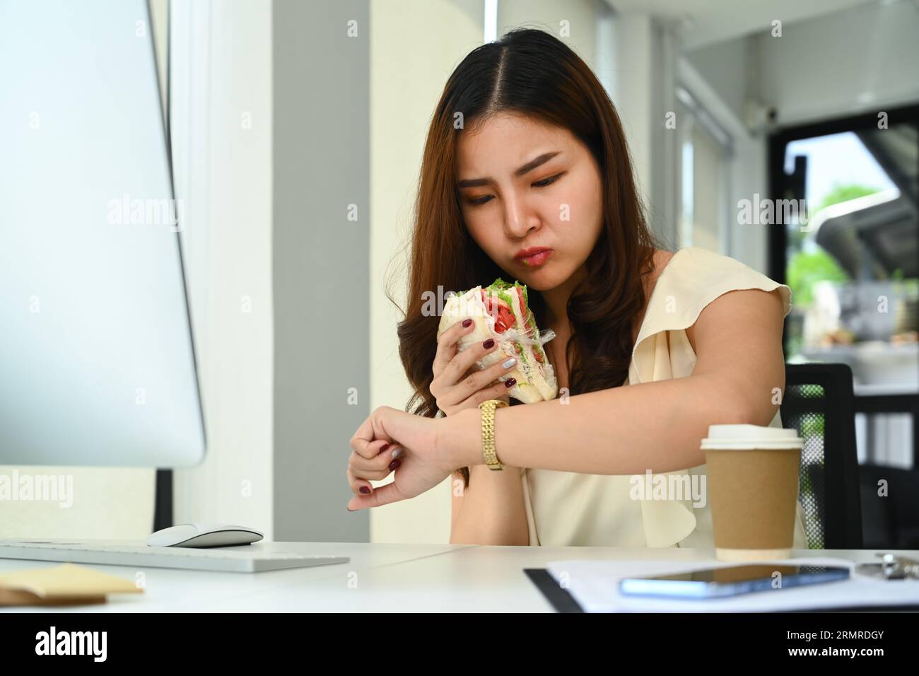 Busy asian female worker eating sandwich and checking time on watch ...