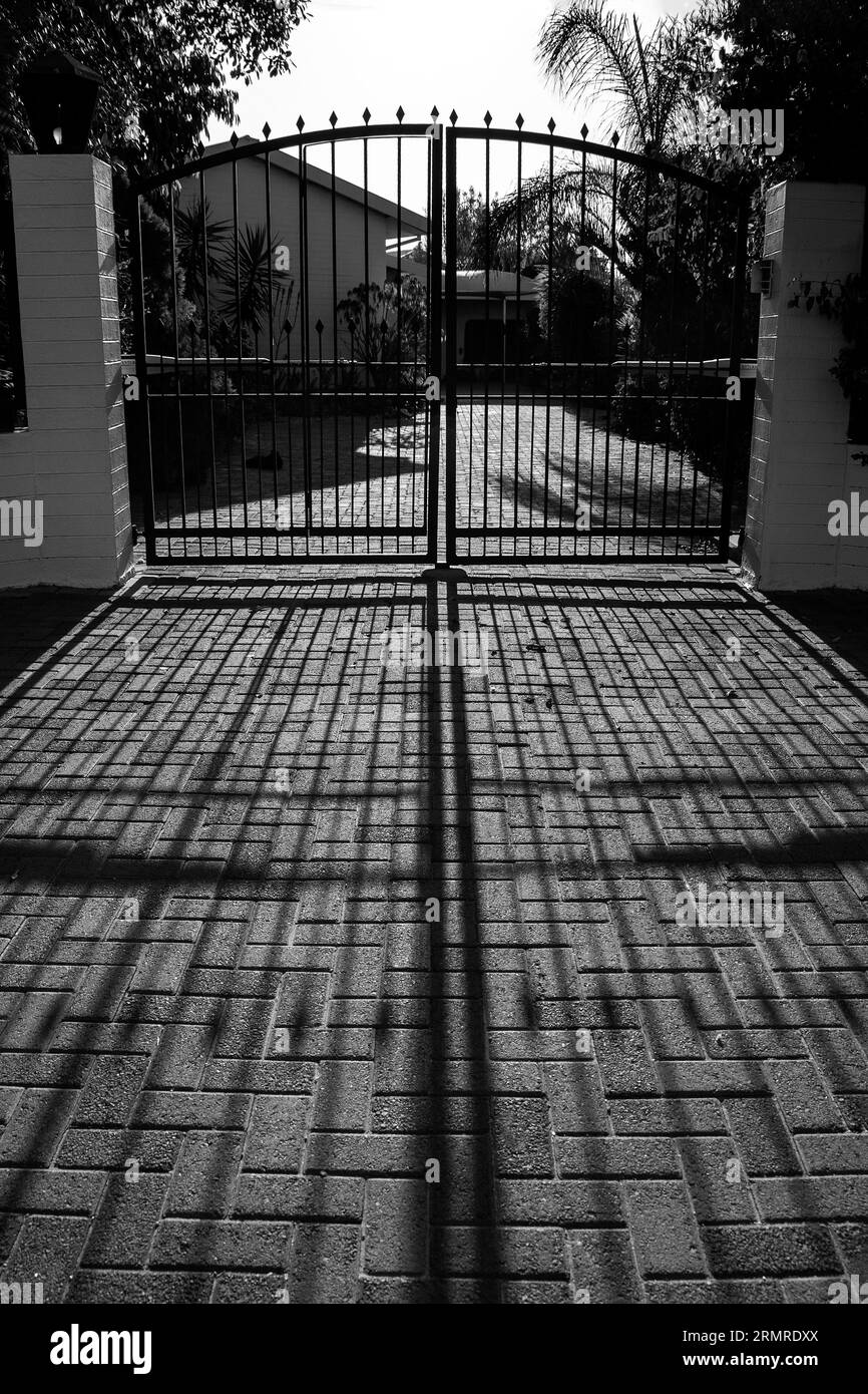 The shadows from a pair of closed; black, sinister wrought iron gates ...