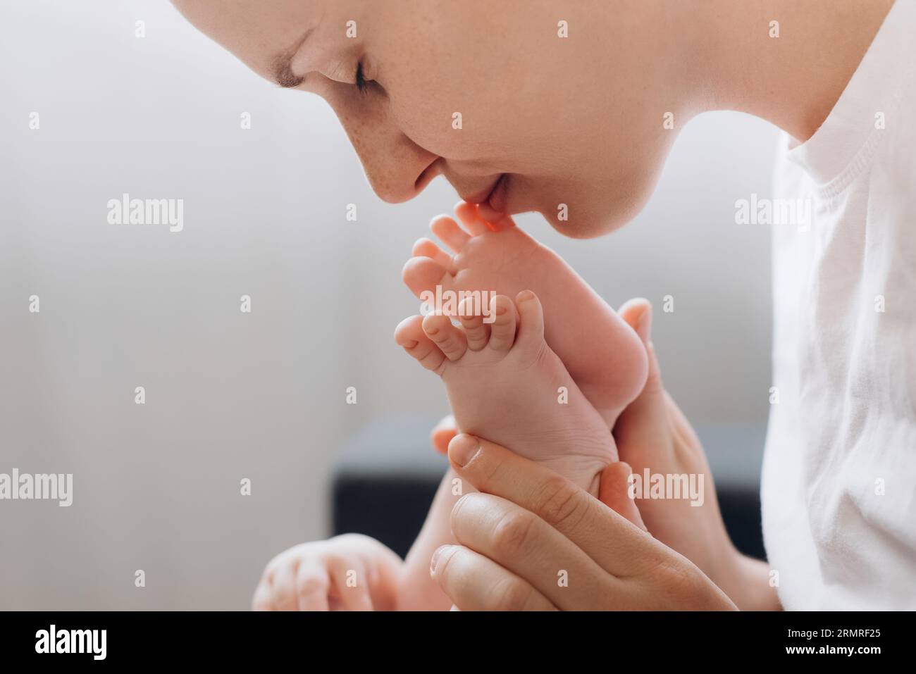 Close up of happy young loving mommy gently kiss little feet sitting on ...