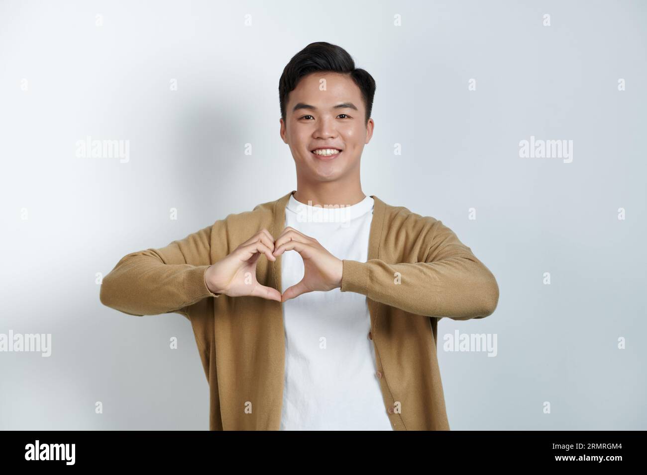 Smiling asian man makes heart gesture demonstrates love sign expresses ...