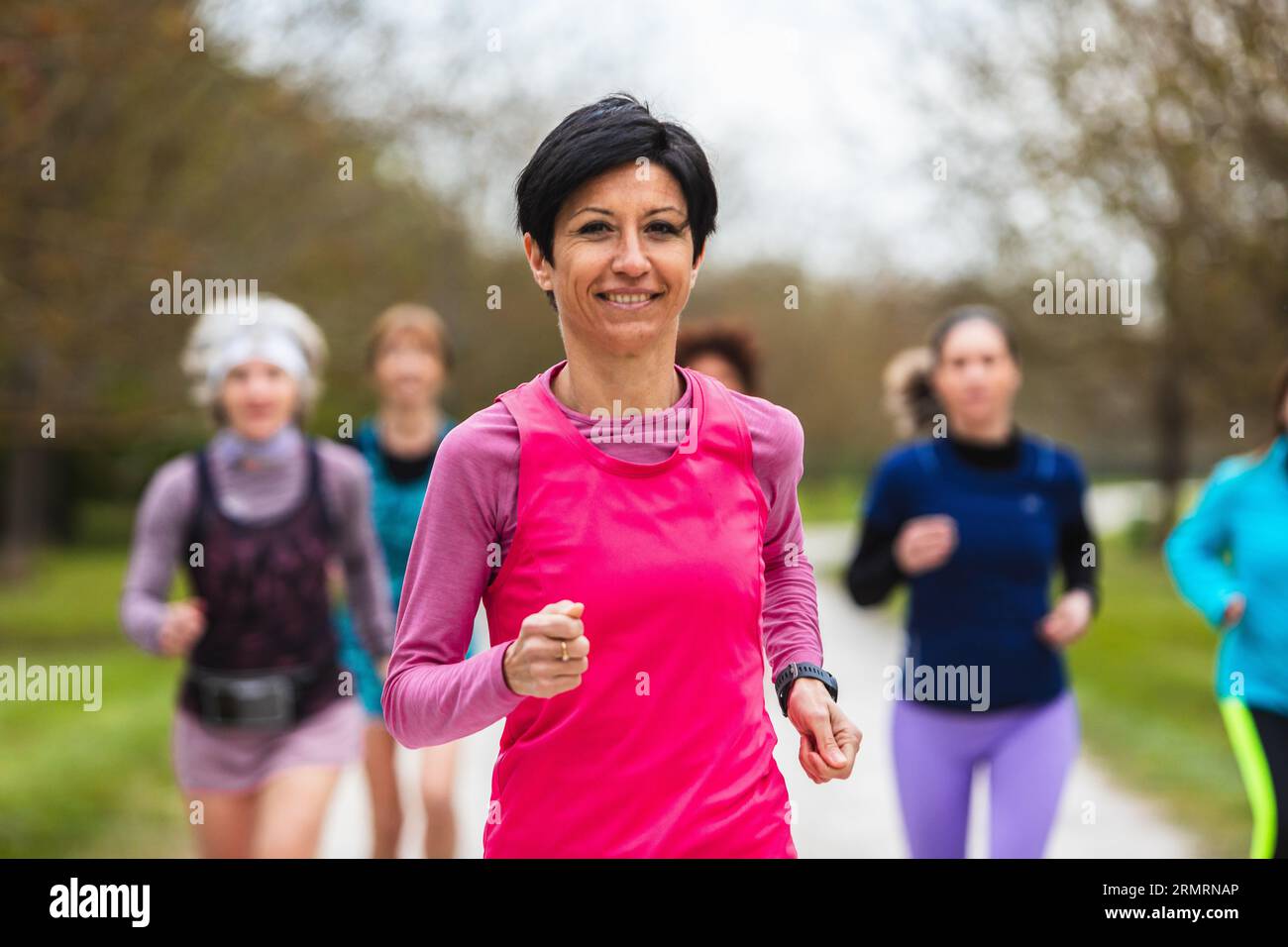 Smiling woman leading a group of female runners training in nature ...