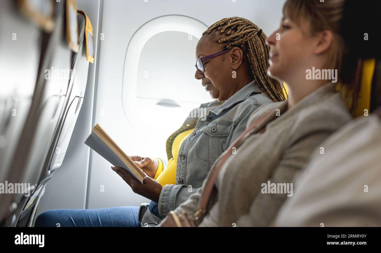African senior woman reading a book while flying on airplane - Travel ...